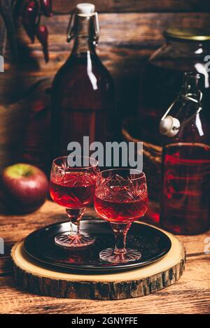 A bottle of vodka, two glasses and a plate of meat snacks on a wooden ...