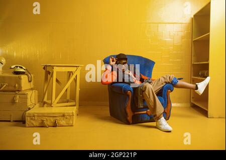 Smiling rapper posing in the chair in studio with yellow tones. Hip-hop ...