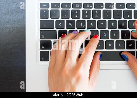Woman fingers with colorful polished nails are typing on a laptop ...