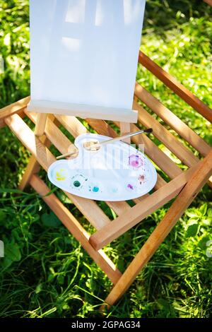 A palette of watercolor multicolored paints stands on a wooden chair ...