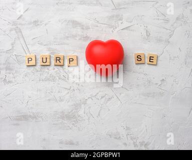 red heart and inscription purpose from wooden blocks on white cement ...