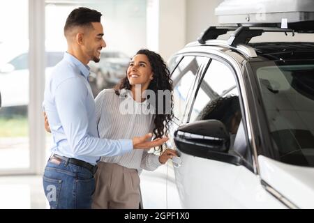 Middle-eastern family choosing new auto, standing by white vehicle ...