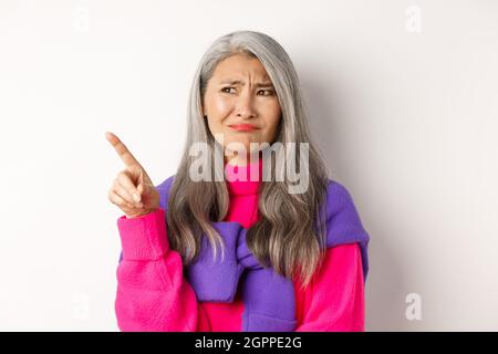 Displeased asian grandmother in pink sweater, grimacing and frowning ...