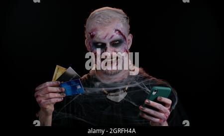 Sinister man Halloween zombie using credit bank card and smartphone ...