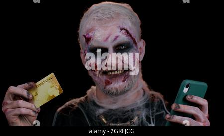Sinister man Halloween zombie using credit bank cards and smartphone ...