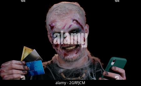 Sinister man Halloween zombie using credit bank card and smartphone ...