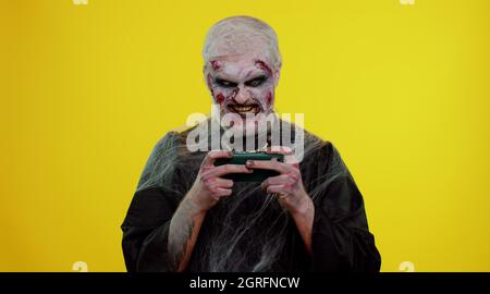 Sinister man Halloween zombie enthusiastically playing racing drive ...