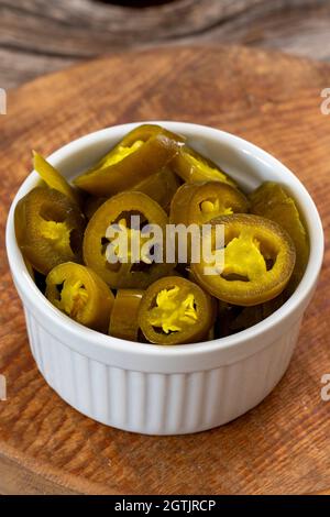 Sliced pickled jalapenos in a white ceramic bowl on a rustic painted ...