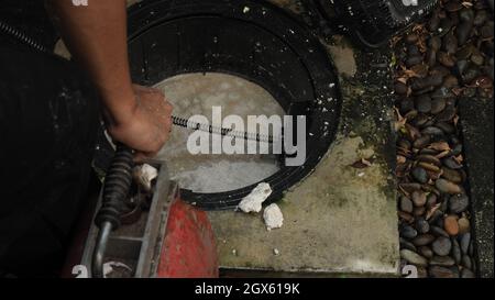 Drain cleaning. Plumber repairing clogged grease trap with auger ...