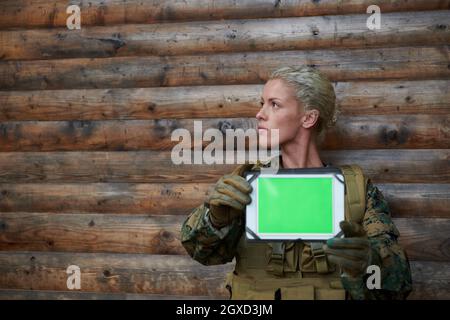 woman soldier using tablet computer against old wooden wall in camp ...