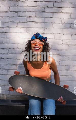 Smiling happy woman hold skateboard on shoulder and pointing finger to ...