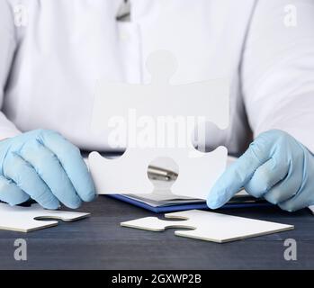 The doctor sits at the table and holds a paper white puzzle. Solution ...