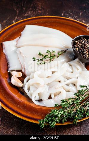 Sliced raw rings squid in a rustic plate with rosemary. Dark background ...