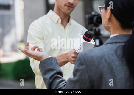 blurred reporter holding microphone near happy asian businesswoman with ...