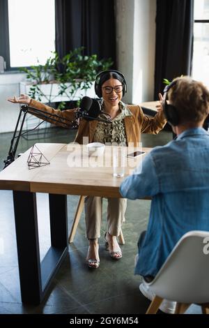 asian radio host in eyeglasses and headphones drinking coffee near ...