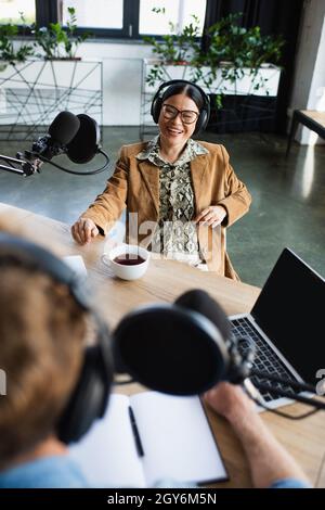 asian radio host in eyeglasses and headphones drinking coffee near ...