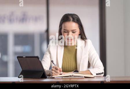 Horizontal shot of a beautiful Asian tutor with tablet, copybook and ...