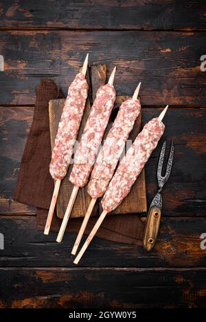 Raw kofta or lula kebabs skewers on a grill with herbs. Dark wooden ...
