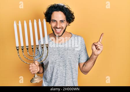 Handsome hispanic man holding menorah hanukkah jewish candle smiling ...