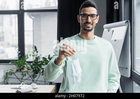 Young Muslim businessman in protective mask looking at colleague during ...