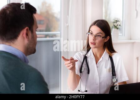 Young female doctor explaining something to a patient at desk in clinic ...