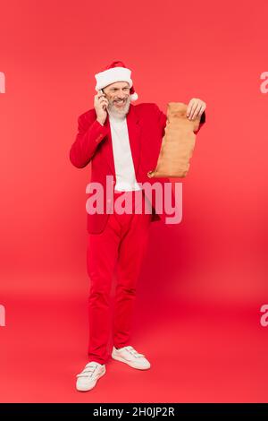 positive mature man in santa hat and red apron hold present Stock Photo ...