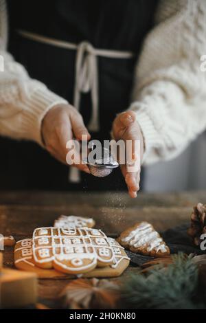 Woman is decorating gingerbread cookies house with white frosting icing ...