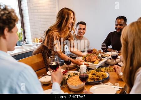 Multiracial happy friends eating turkey during thanksgiving dinner at ...