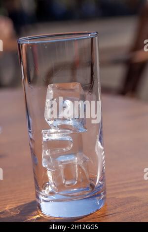 Glass with ice pieces on the wooden table. Ice starting to melt ...