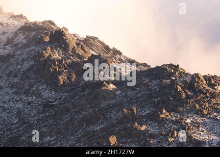 Rough stones covered with moss and bushes located on top of snowy ...