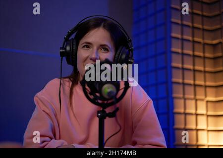 Positive young female radio host in casual clothes and headphones ...