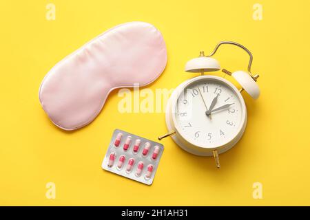 Stylish sleep mask, alarm clock and cosmetic jar on color background ...