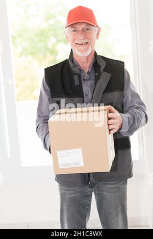 Portrait of smiling senior deliverer holding a package; panoramic ...