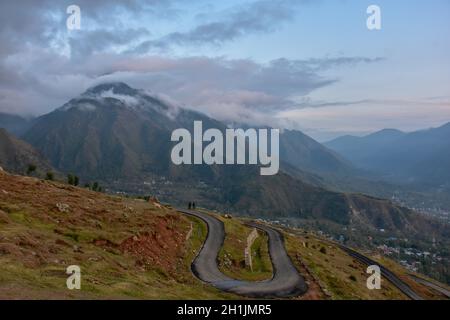 Srinagar, India. 18th Oct, 2021. A man carries hay as he walks down a hill during a cloudy day ...