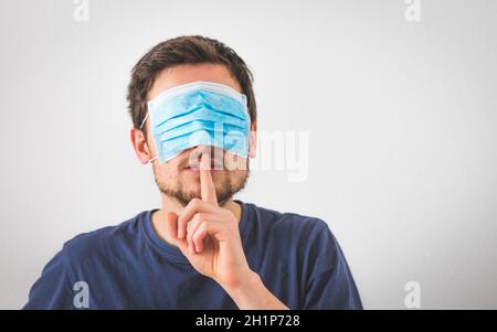 Young angry man with face mask over the eyes is doing a psst! gesture ...
