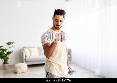 Strong young Arab man exercising with dumbbells at home. Domestic ...