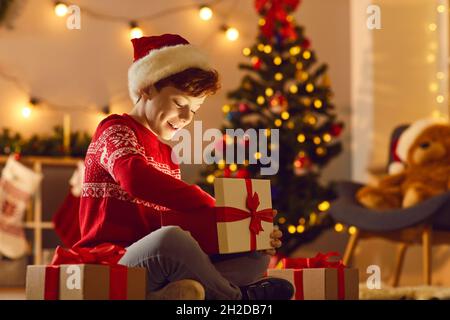 Smiling boy looks in present box wearing Santa hat Stock Photo - Alamy