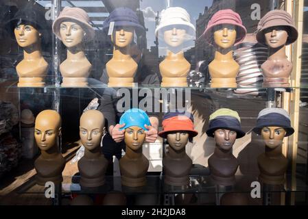 A shopkeeper fits and adjusts the hats on female mannequin heads in the ...