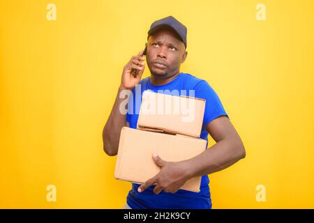 African dispatch man making a call with a smartphone, carrying boxes ...