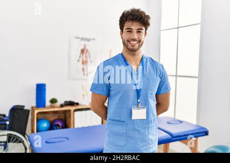 Young hispanic man wearing physio therapist uniform using touchpad at ...