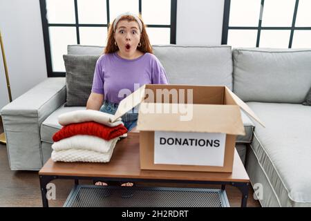 Young redhead woman putting used clothes into donations box smiling ...