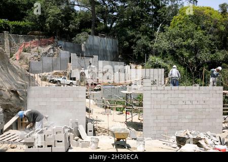 Workers build concrete retaining wall using gray blocks in residential ...