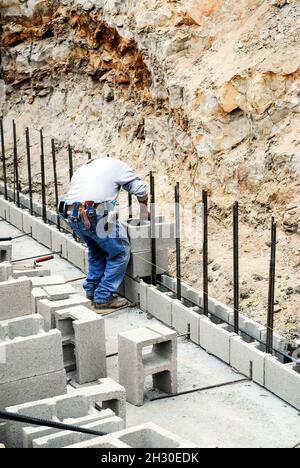 Workers build concrete retaining wall using gray blocks in residential ...