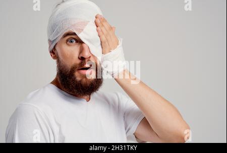 bearded man with bandaged head and eye hospitalization light background ...