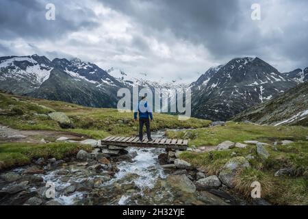 Man hiker resting on small bridge over mountaian river at Schlegeis ...