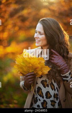 Hello october. smiling modern woman in brown coat with autumn yellow ...