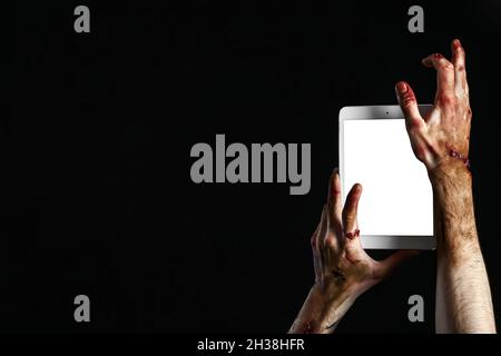 Hands of zombie with tablet computer on dark background. Happy ...