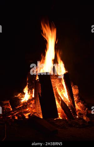Wood logs burning during a dark night, producing orange flames and ...