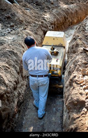 Construction worker operating a soil compactor in a deep trench Stock ...