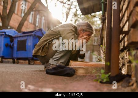 Street life, homeless man squating to wash face Stock Photo - Alamy